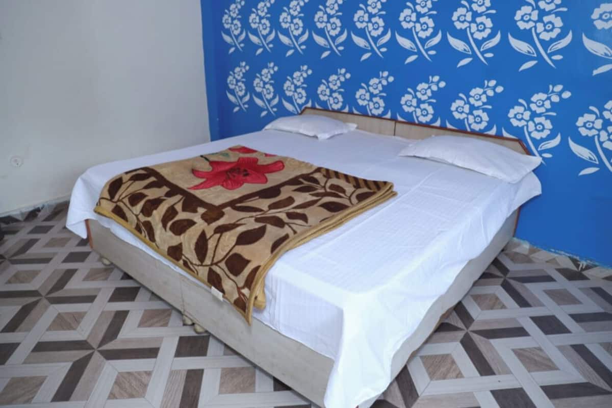 Cama com colcha estampada e almofadas brancas, diante de uma parede azul com papel de parede floral.