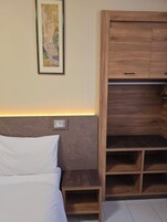 Quarto com cama, mesa de cabeceira, guarda-roupa de madeira e uma obra de arte emoldurada na parede.