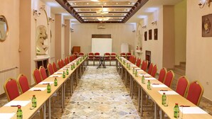 Uma sala de conferência com uma mesa comprida, cadeiras vermelhas e um candelabro.
