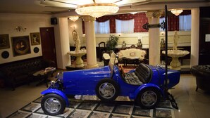 Um hall de entrada com um carro vintage azul, um candelabro e decoração clássica.