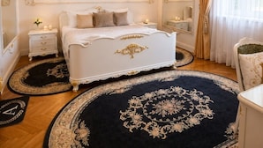 Quarto com cama grande, lustre, duas luminárias de parede, espelho e janela com cortinas.