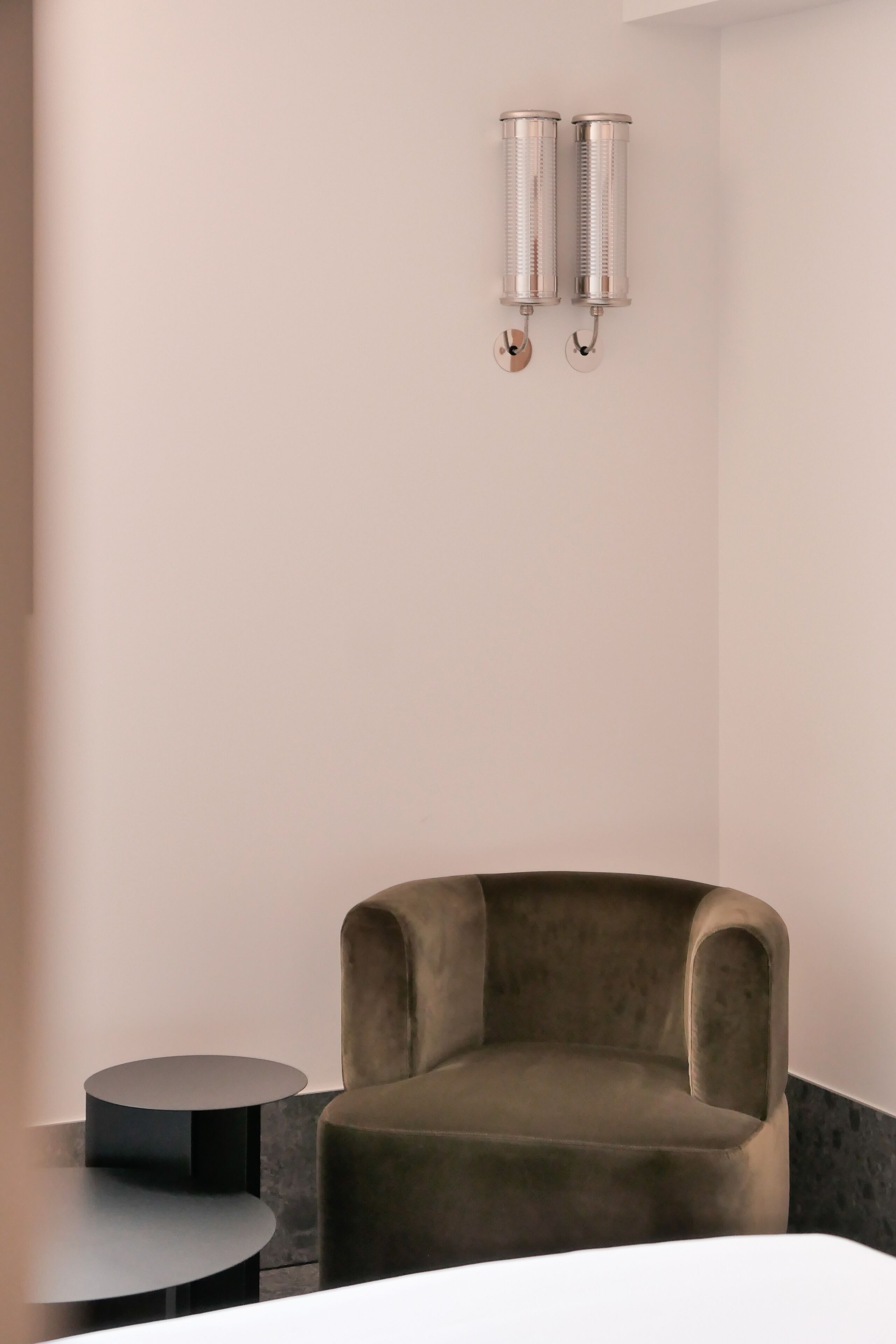 Quarto moderno com uma poltrona confortável, uma pequena mesa redonda e dois objetos cilíndricos fixados na parede.