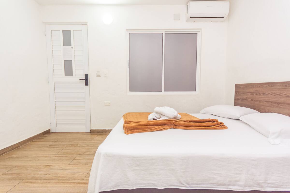 Quarto com cama, janela, porta e aparelho de ar condicionado.