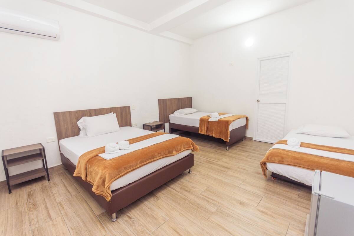 Quarto de hotel com duas camas, uma pequena mesa de cabeceira, um guarda-roupa e uma porta branca.