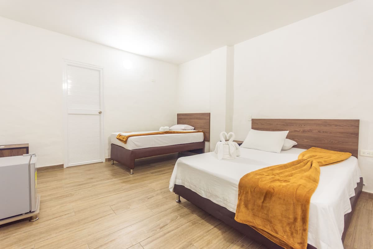 Quarto de hotel com duas camas, um guarda-roupa e uma pequena cozinha equipada.