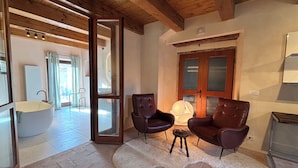 Quarto com uma banheira grande, duas poltronas de couro, um tapete branco e teto de madeira.