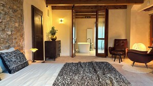 Quarto com cama, penteadeira, cadeira, luminária e banheiro visível por uma porta aberta.