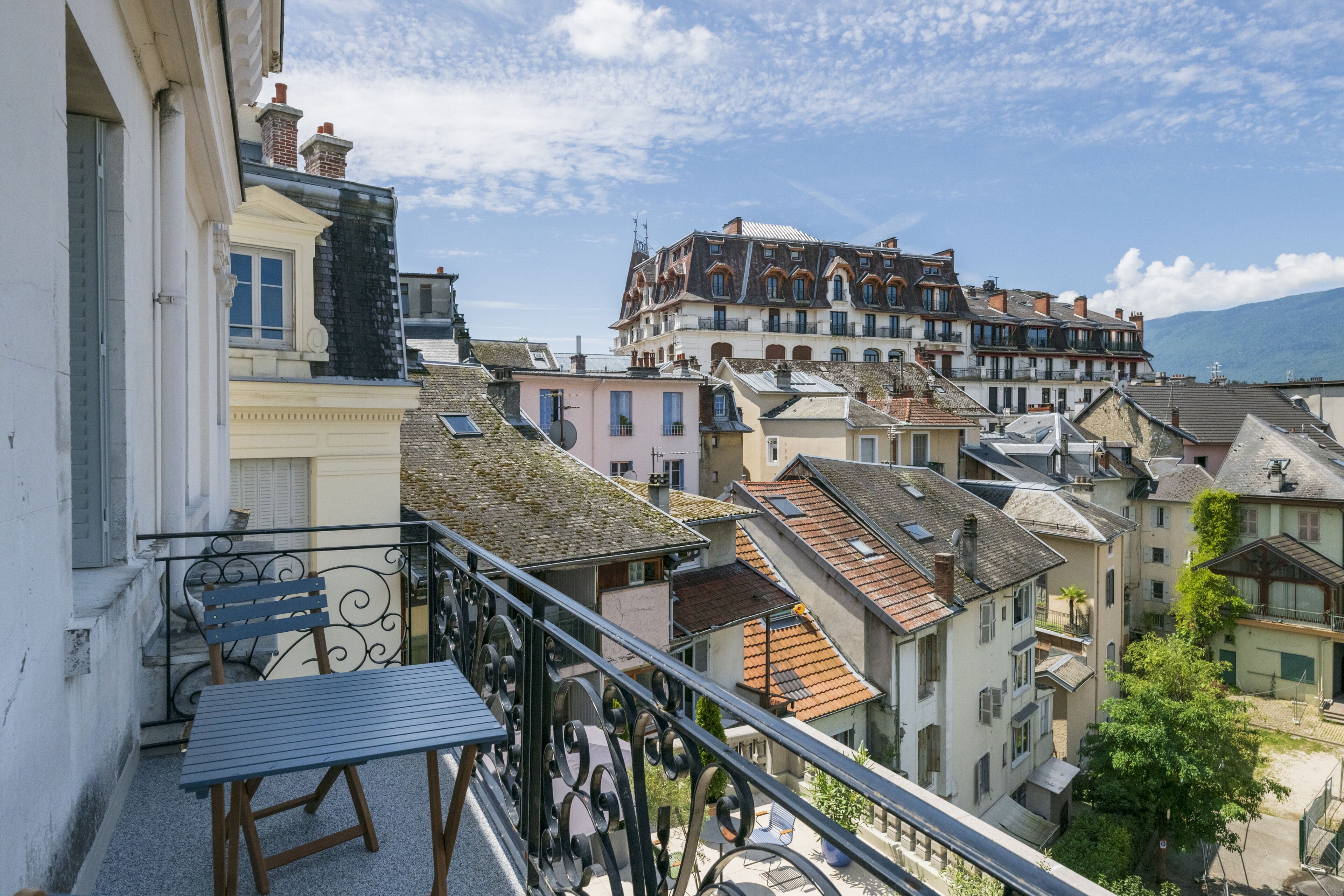 Varanda com mesa e cadeiras, com vista para uma fileira de edifícios coloridos e uma montanha ao fundo.