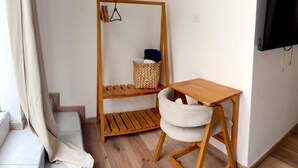 Quarto com um banco de madeira, uma mesinha, televisão e janela com cortinas.