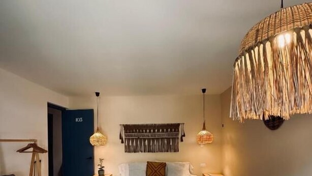 Quarto com cama, mesas de cabeceira, luminária pendente e porta com a inscrição 'K03'.