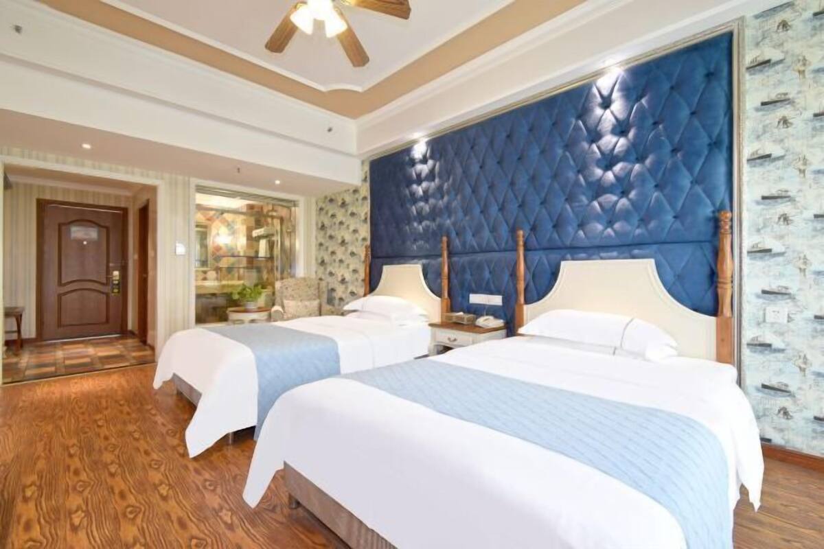 Quarto de hotel com duas camas, uma cabeceira grande e estofada, piso de madeira e uma porta que dá para o banheiro.