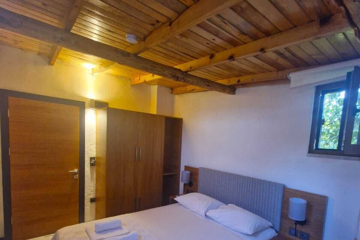 Quarto de hotel com teto de madeira, cama com roupa de cama branca, mesa de cabeceira e armário.