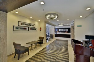 Um hall de hotel com piso xadrez, área de estar e balcão de recepção.
