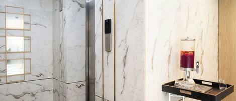 Um banheiro com piso de mármore, um dosador de vidro, um espelho e um elevador.