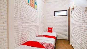Um quarto pequeno com paredes de tijolo branco, duas camas com roupa de cama vermelha e branca, e uma janela.