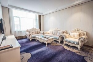 Quarto de hotel com uma janela grande, um conjunto de sofás, uma mesa de centro e uma TV de tela plana.