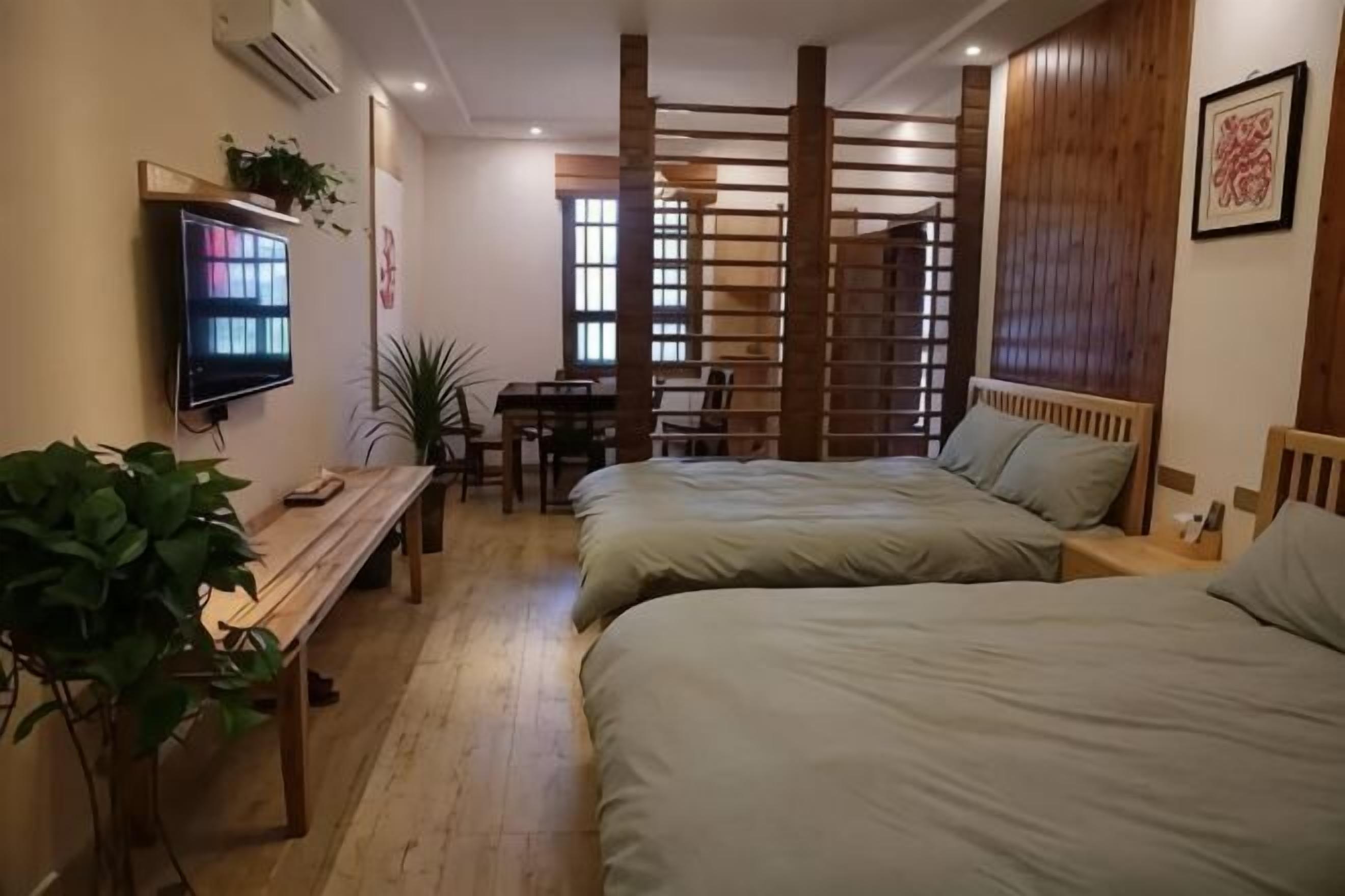 Quarto de hotel com duas camas, uma escrivaninha, uma cadeira, uma televisão e uma planta.