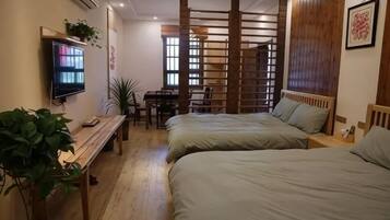 Quarto de hotel com duas camas, uma escrivaninha, uma cadeira, uma televisão e uma planta.