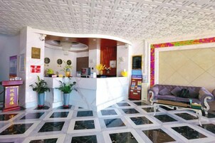 Uma área de recepção de hotel com um balcão curvo, um balcão de atendimento, um sofá e uma máquina de vendas.
