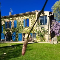 Uma casa tradicional com telhado de telhas, janelas com contraventanas azuis e um jardim com um banco.