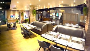 Um restaurante com cabines e mesas, uma área de cozinha e uma tela de televisão.