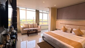 Quarto de hotel moderno com uma cama grande, um sofá, uma televisão e vista para o campo.
