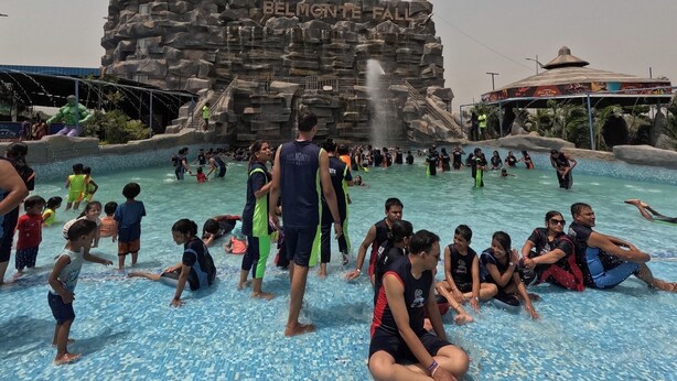Um parque aquático com uma grande formação rochosa identificada como "BELMONTE FALL" e uma área de piscina onde pessoas aproveitam a água.