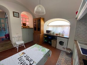 Uma cozinha compacta com máquina de lavar, micro-ondas e pia. Há uma pequena área de refeições com uma cadeira e uma mesa.