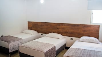 Quarto de hotel com três camas de solteiro, cabeceiras de madeira e uma janela grande com vista.