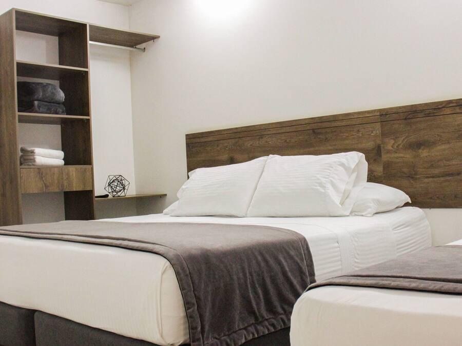 Quarto de hotel com duas camas, cabeceira de madeira e prateleira embutida com toalhas dobradas.