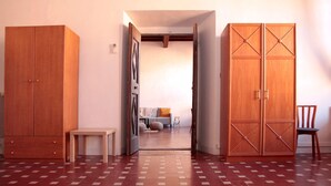 Um quarto com chão quadriculado, guarda-roupa de madeira e uma mesa pequena.