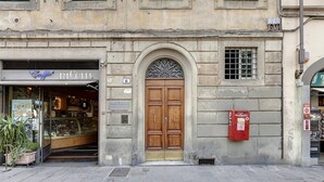 Um edifício com uma loja chamada "RICCI" no andar térreo, com uma porta dupla de madeira e uma pequena janela acima.