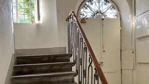 Uma escadaria com corrimão de madeira e balaústres de metal, conduzindo a uma porta com vitrais decorativos acima.