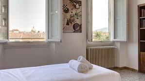 Quarto com cama, radiador, janela com persianas abertas e um quadro na parede.