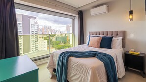 Quarto de hotel moderno com uma cama grande, vista para a cidade e ar condicionado na parede.