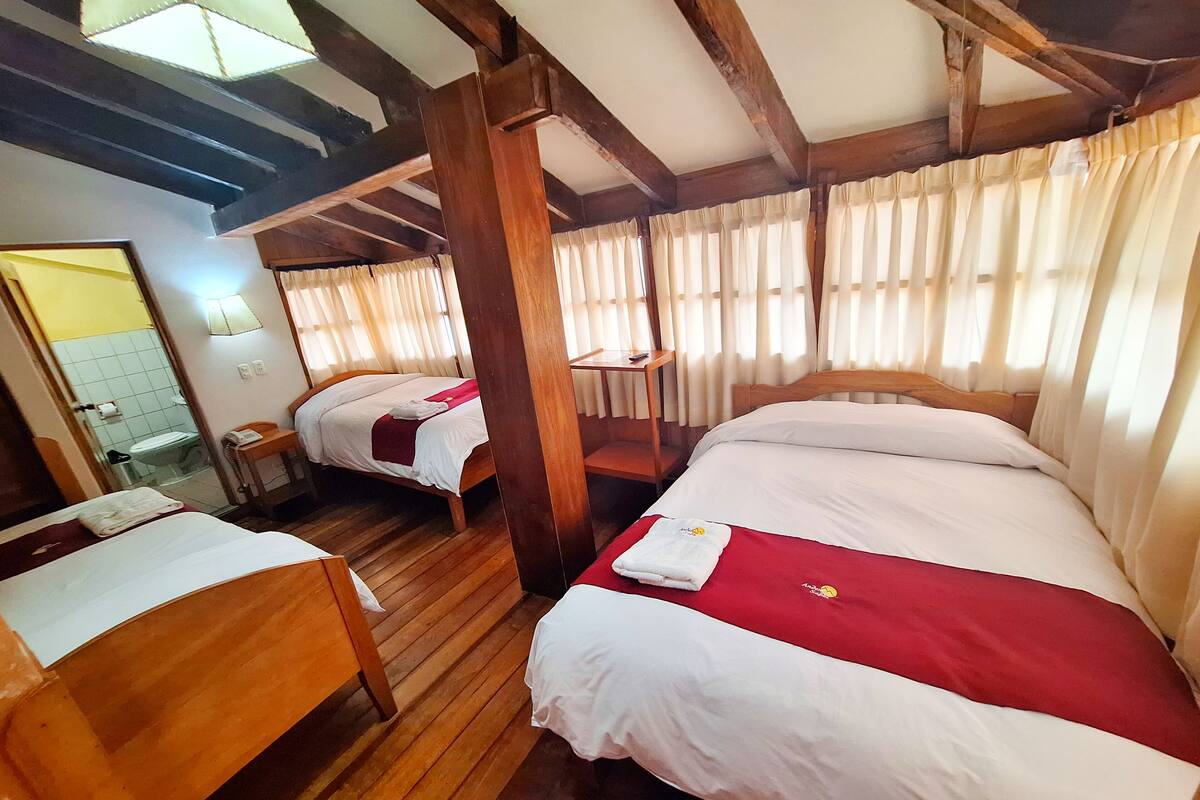 Quarto de hotel com duas camas, soalho de madeira e estrutura de teto em madeira.