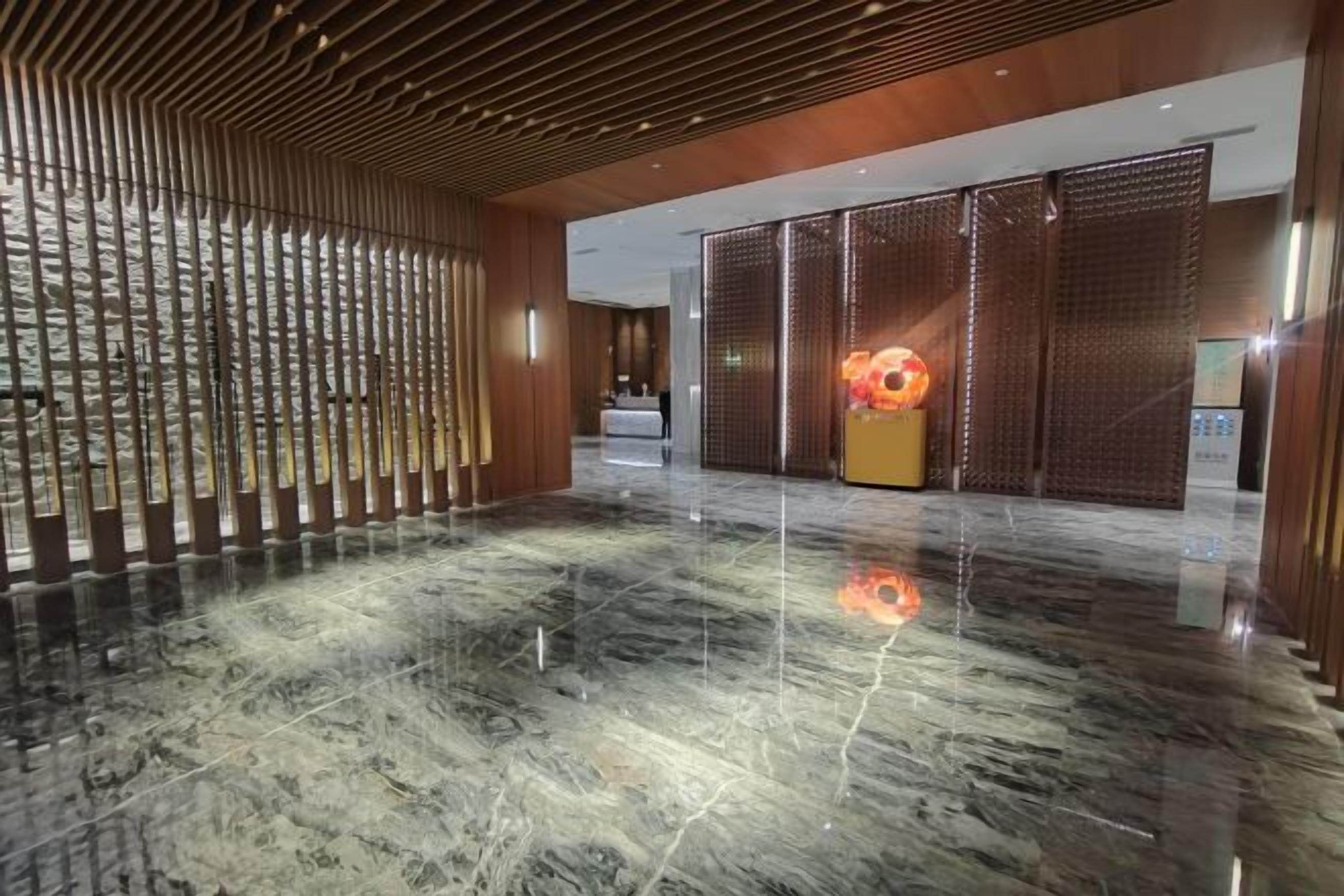 Um hall com piso de mármore polido, painéis de madeira e uma área de recepção com um display digital.