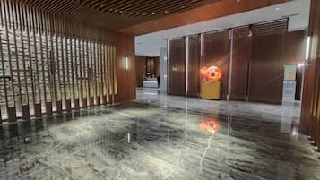 Um hall com piso de mármore polido, painéis de madeira e uma área de recepção com um display digital.