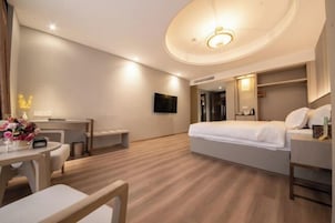 Quarto de hotel com cama, escrivaninha, cadeira, televisão e uma pequena mesa com flores.