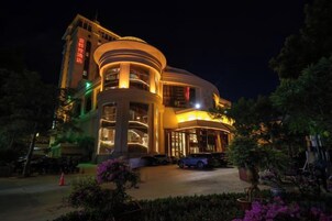 Um hotel de vários andares com fachada curva, entrada iluminada e área de estacionamento com um carro.