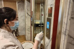 Uma pessoa operando o painel de controle de um elevador em um corredor com piso de mármore.
