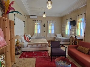 Quarto de hotel com cama, dois sofás, uma cadeira, televisão e janela com cortinas.