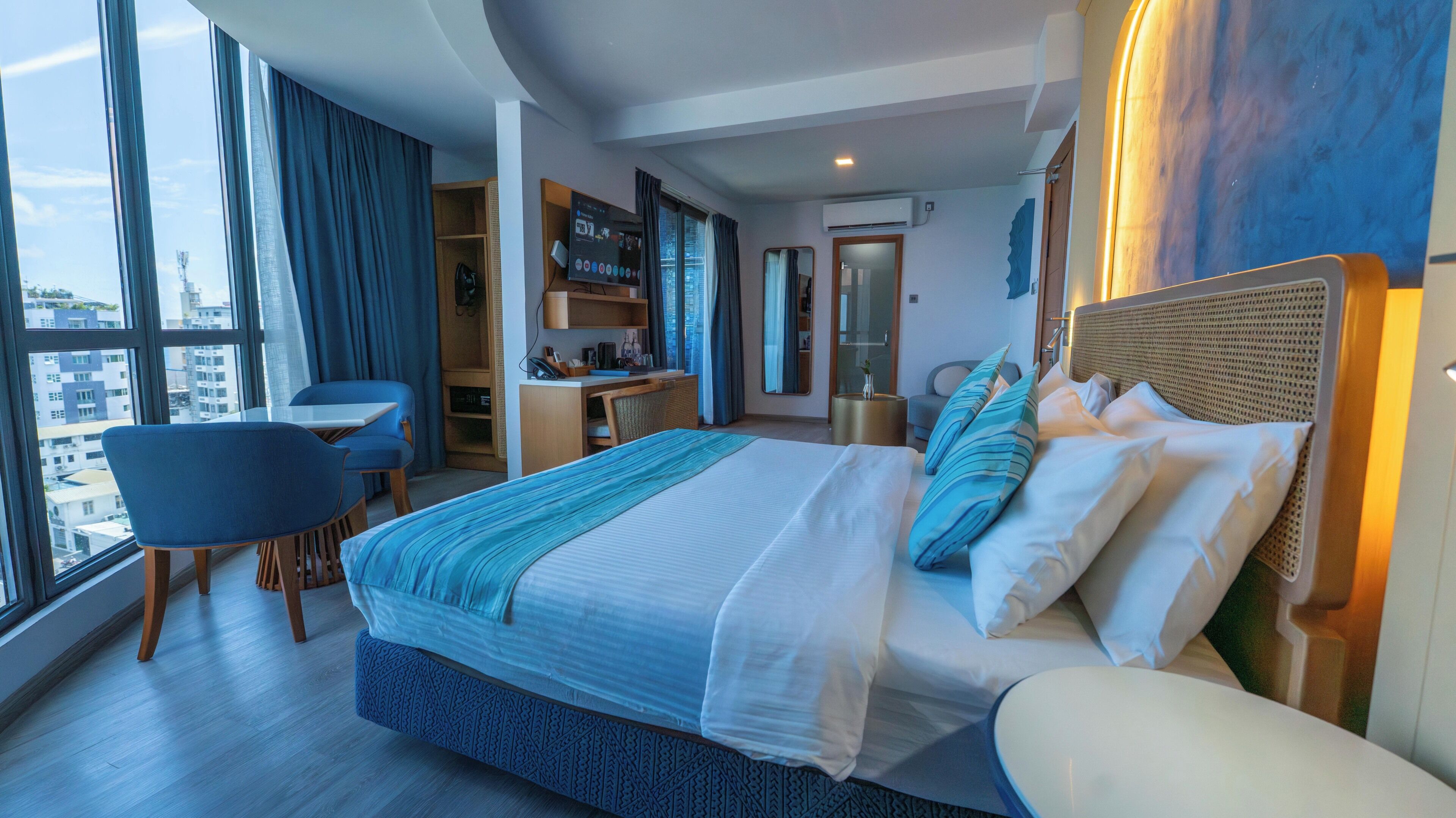 Quarto de hotel com cama, escrivaninha, cadeira e vista para a cidade.