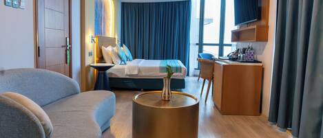 Quarto de hotel moderno com cama, sofá, escrivaninha e mesa de centro redonda.