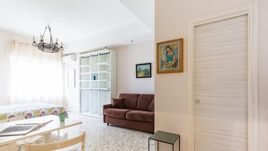 Um quarto com uma cama, um sofá marrom, uma mesa pequena, uma cadeira, uma estante de livros e uma porta.