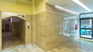 Interior de elevador moderno, com piso de mármore e porta de vidro que dá para uma área externa.