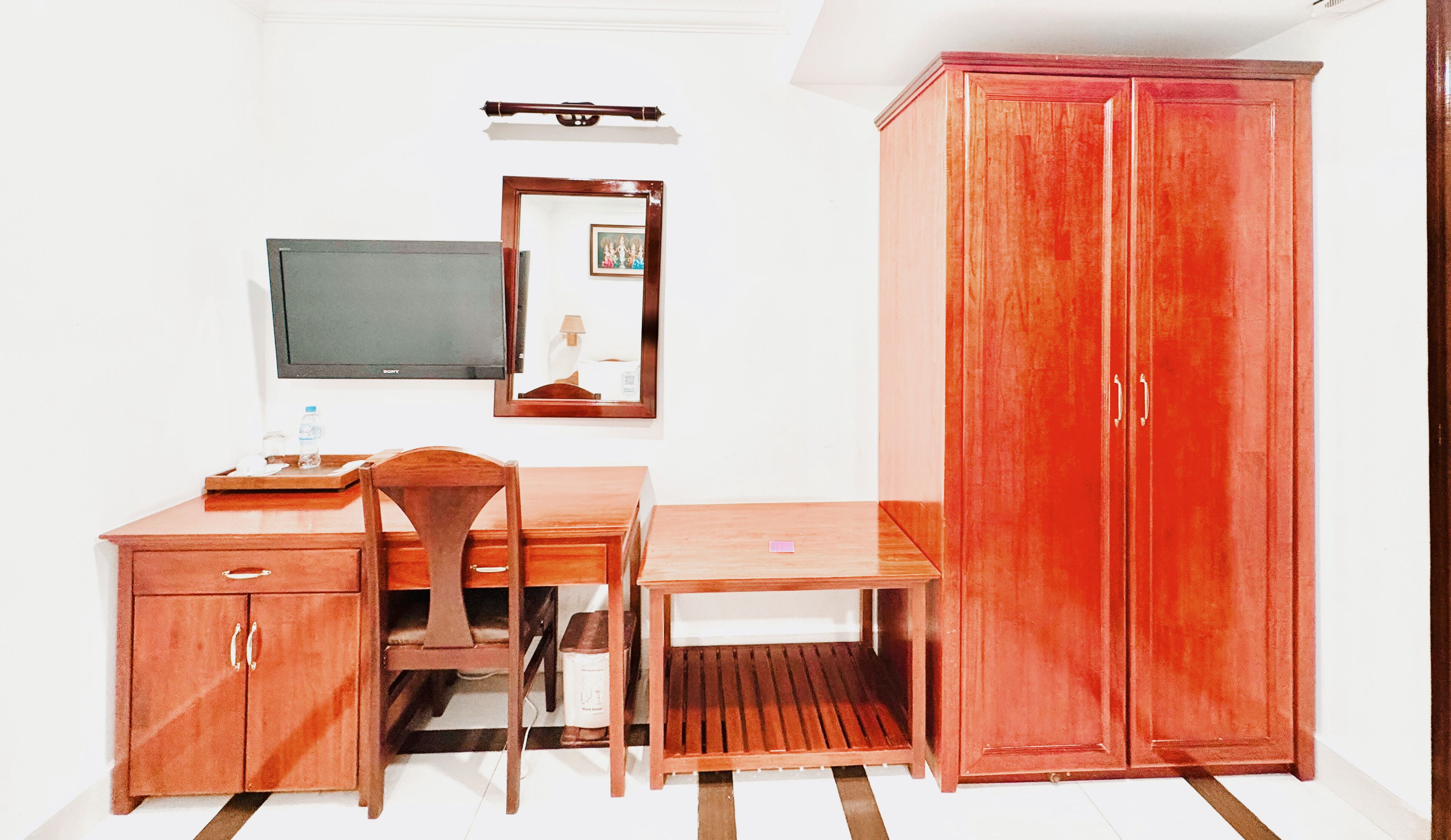 Quarto com escrivaninha, cadeira, guarda-roupa e televisão.