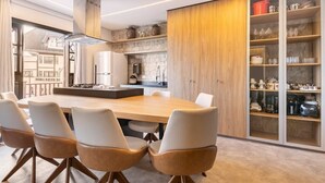Uma cozinha moderna com mesa e cadeiras de madeira, forno embutido e armário de vidro com louças.