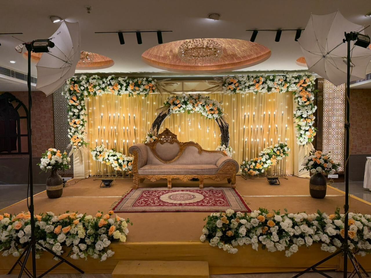 Um palco com um sofá, arranjos florais e equipamentos de iluminação.