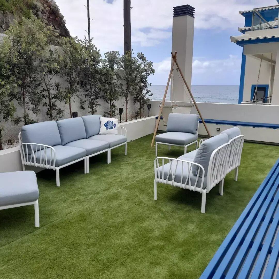 Um terraço com sofá, cadeiras e balanço, com vista para o mar.